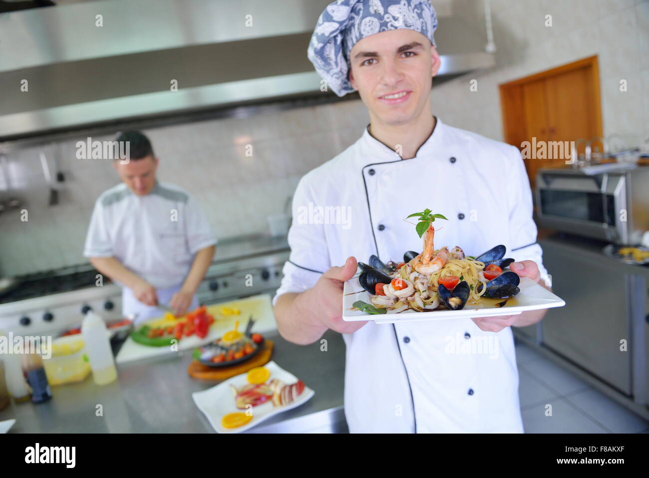 Handsome chef dressed in white uniform decorating pasta salad and ...