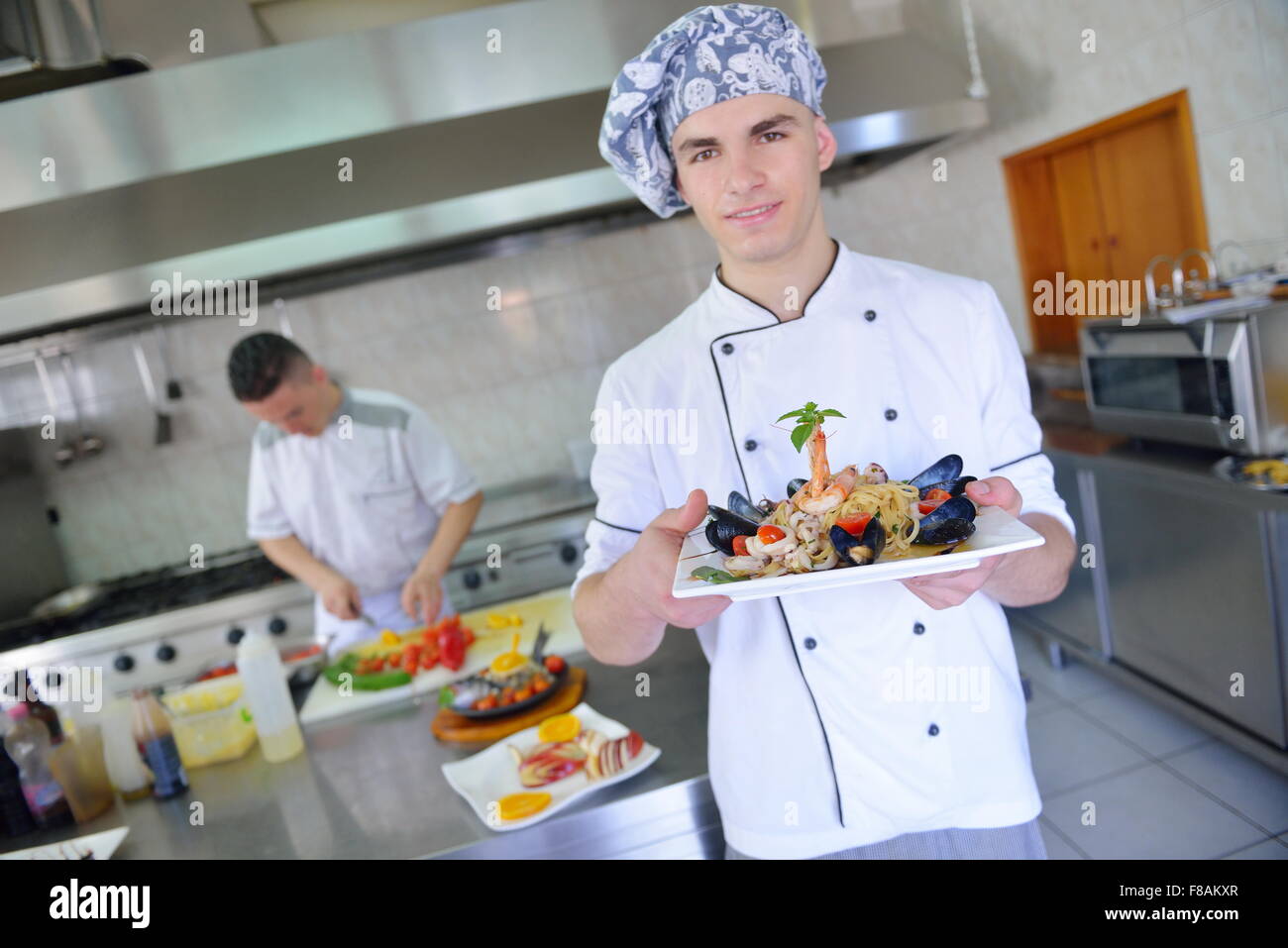 Handsome chef dressed in white uniform decorating pasta salad and ...