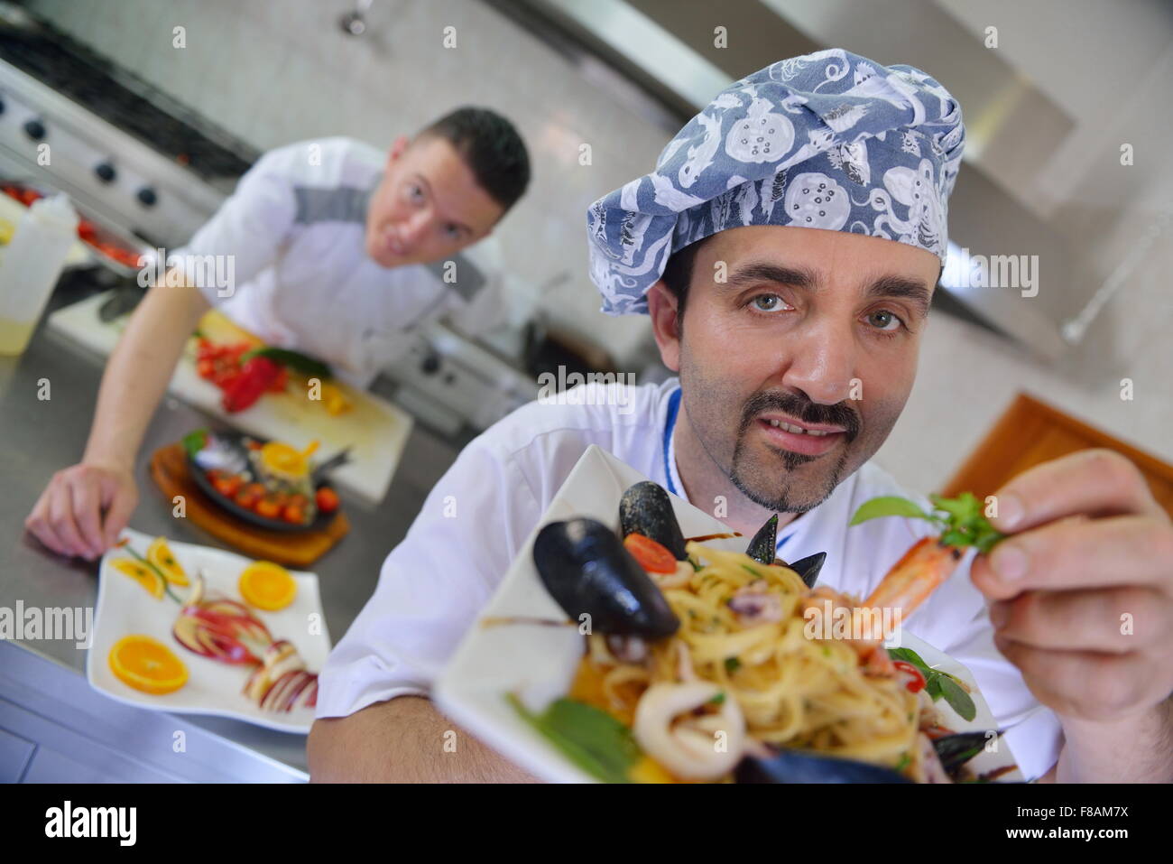 Handsome chef dressed in white uniform decorating pasta salad and ...
