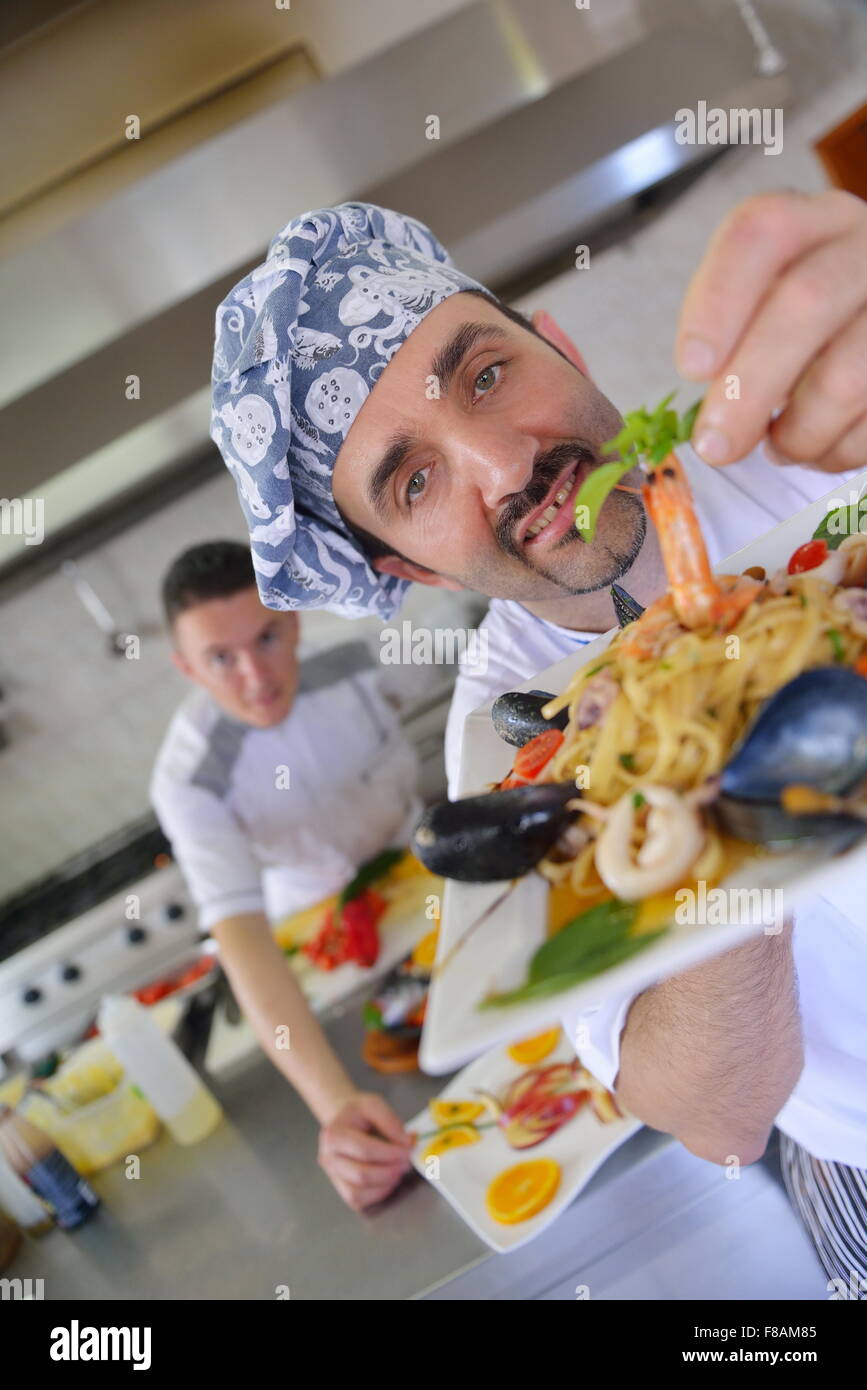 Handsome chef dressed in white uniform decorating pasta salad and ...