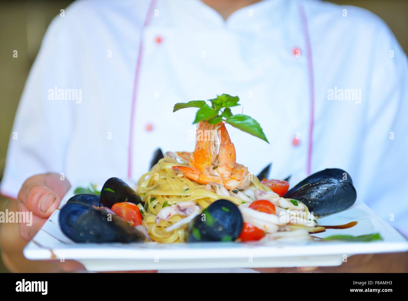Handsome chef dressed in white uniform decorating pasta salad and ...
