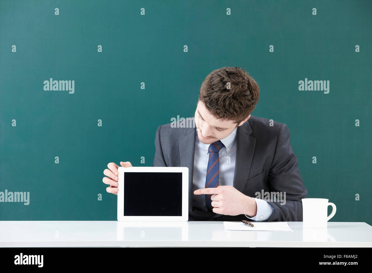 Portrait of man in suit looking down at tablet and pointing at it with ...