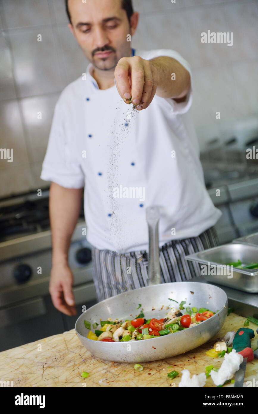 Handsome chef dressed in white uniform decorating pasta salad and ...