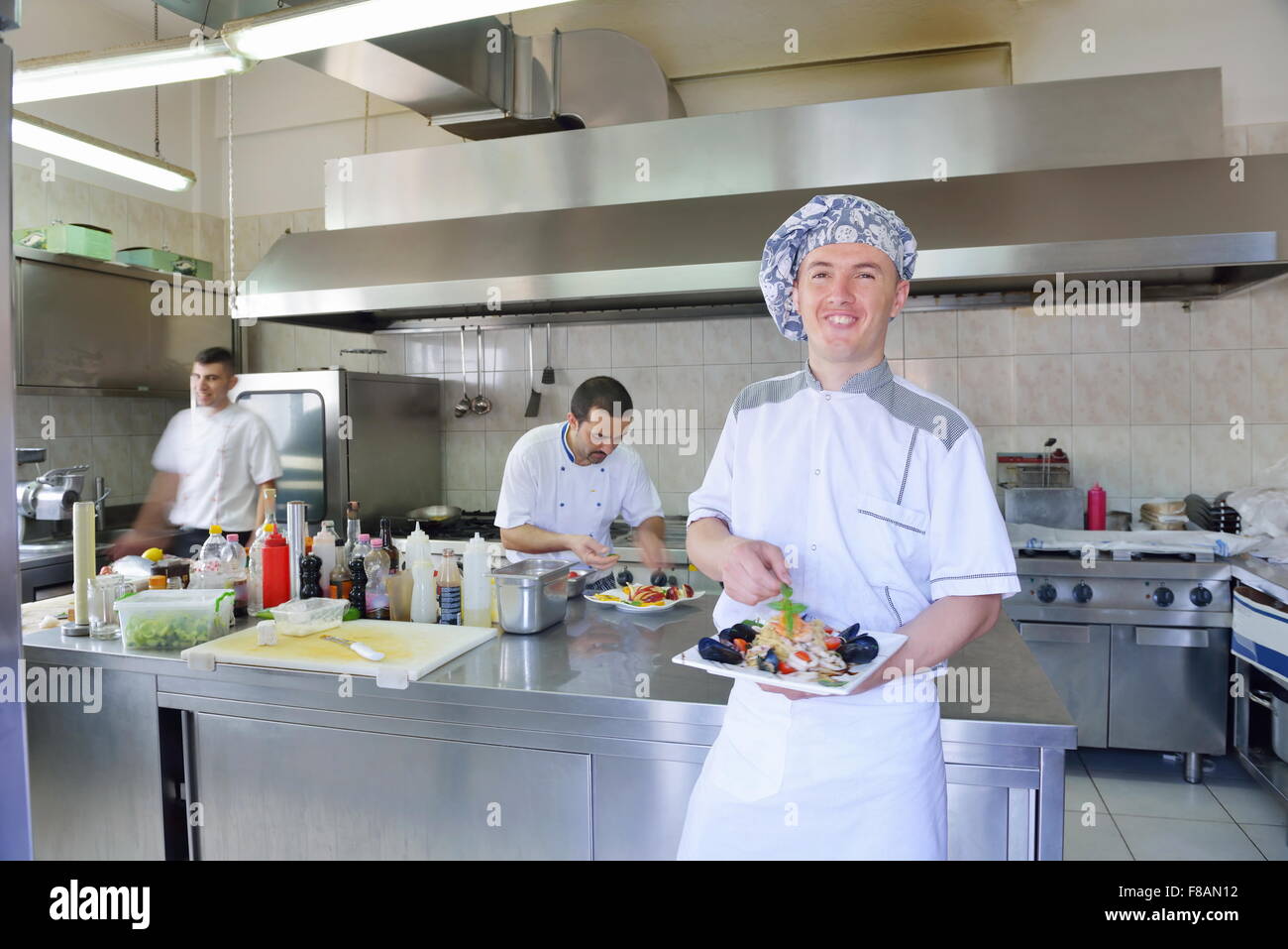 Handsome chef dressed in white uniform decorating pasta salad and ...