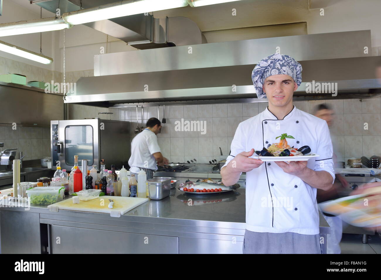 Handsome chef dressed in white uniform decorating pasta salad and ...