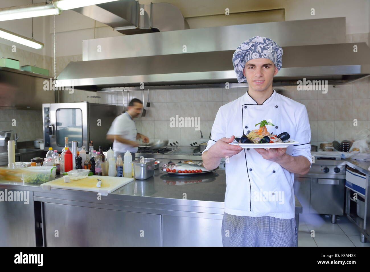 Handsome chef dressed in white uniform decorating pasta salad and ...