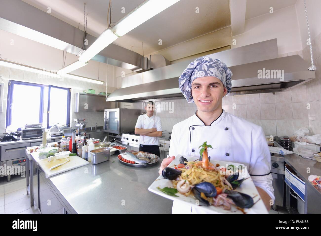 Handsome chef dressed in white uniform decorating pasta salad and ...
