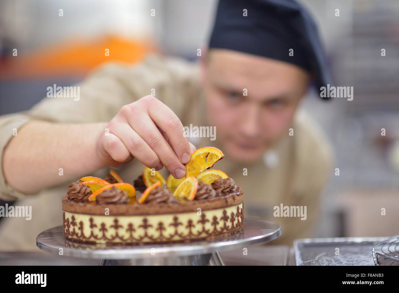 Closeup of a concentrated male pastry chef decorating dessert cake food ...
