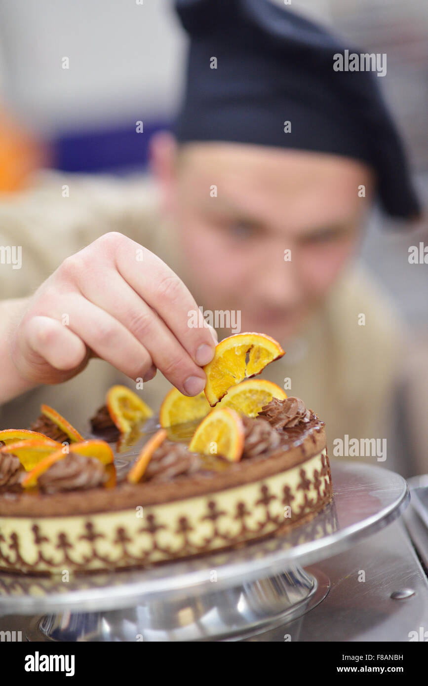 Closeup of a concentrated male pastry chef decorating dessert cake food ...