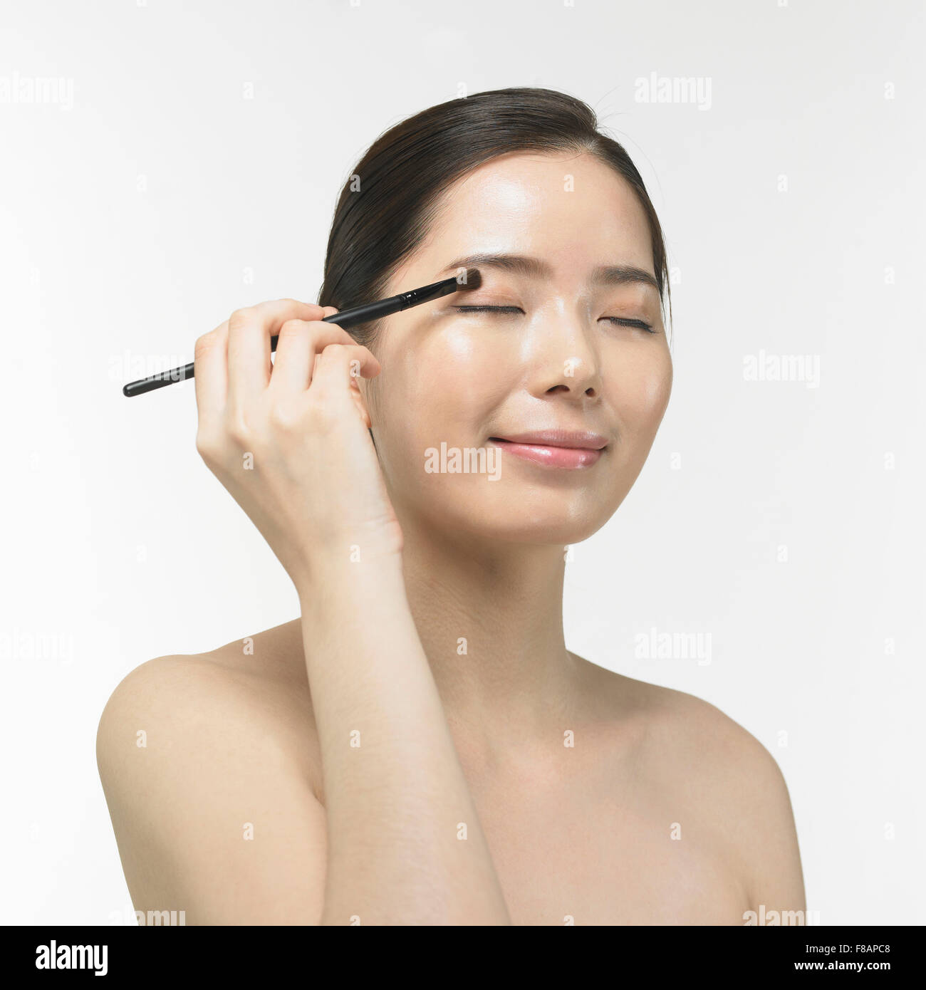 Portrait of smiling Korean woman closing her eyes and applying eye shadow with brush Stock Photo ...
