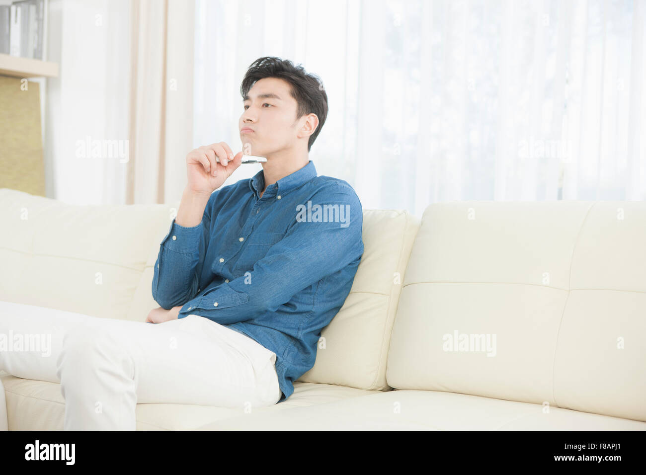 Young man looking bored sitting on sofa Stock Photo - Alamy