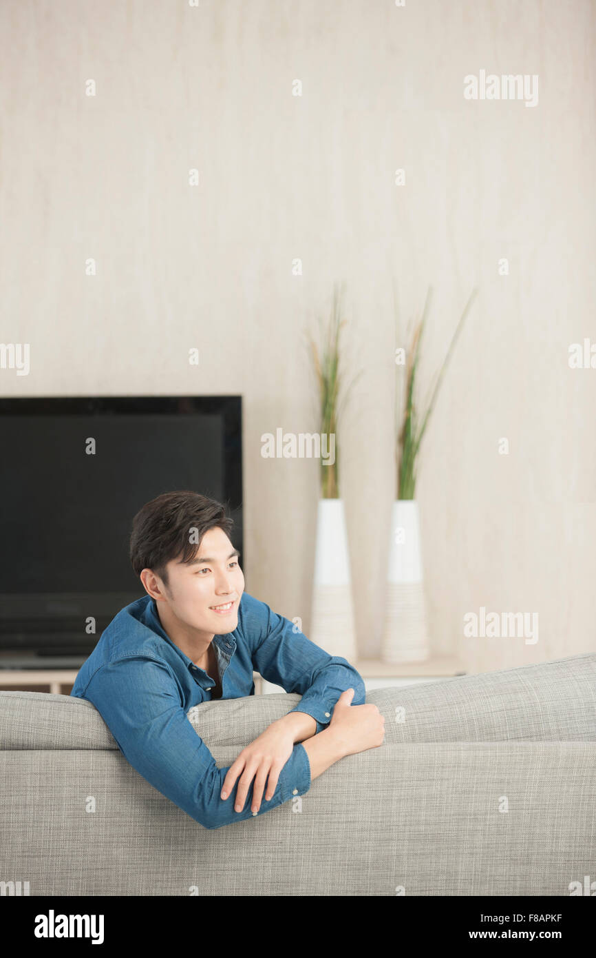 Side view portrait of smiling young man on sofa against TV Stock Photo ...