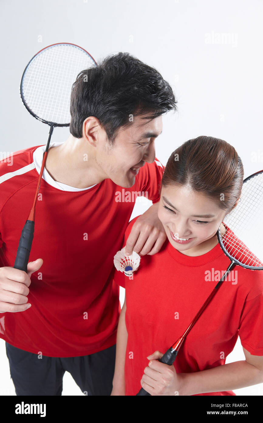 Portrait of smiling couple talking in a whisper with badminton rackets ...