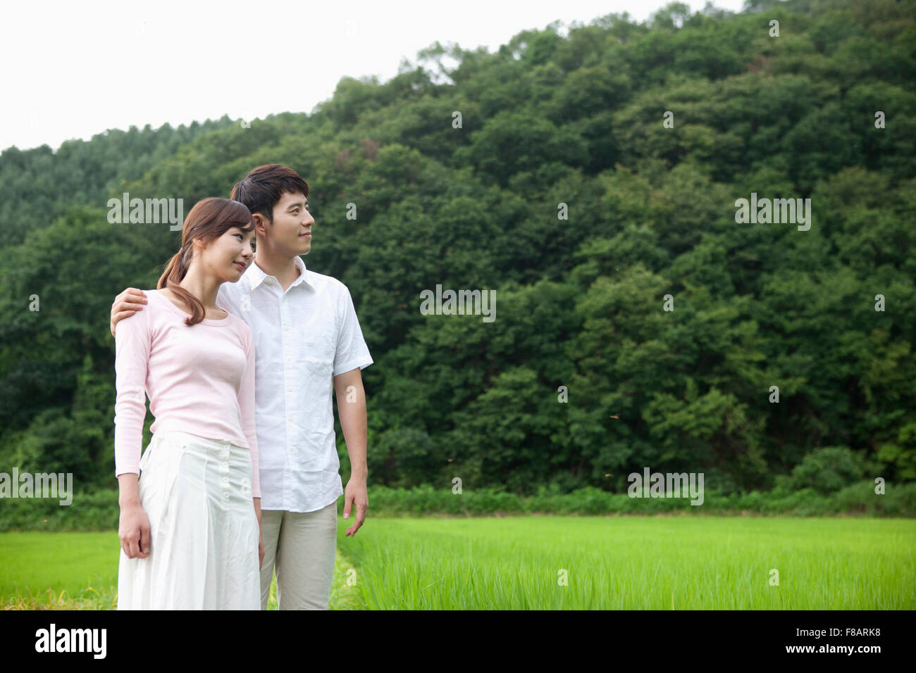 Smiling couple placing hand on shoulder looking up against rice fields ...