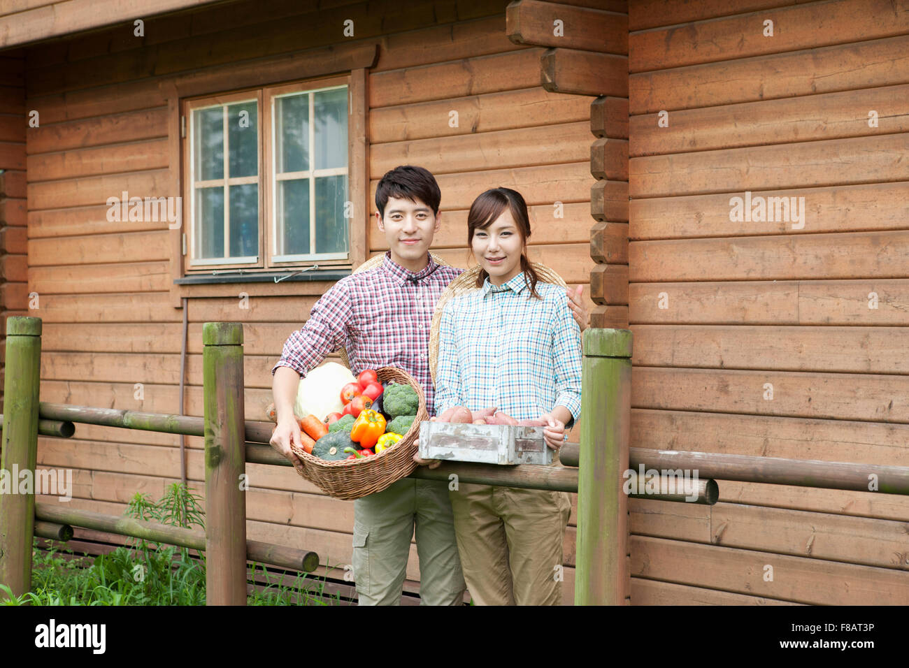 Smiling couple standing with fresh vegetables in front of country house ...