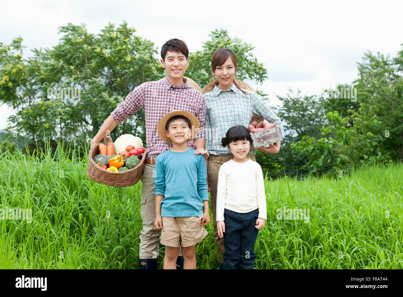 Smiling family standing with fresh vegetables staring at front in the ...
