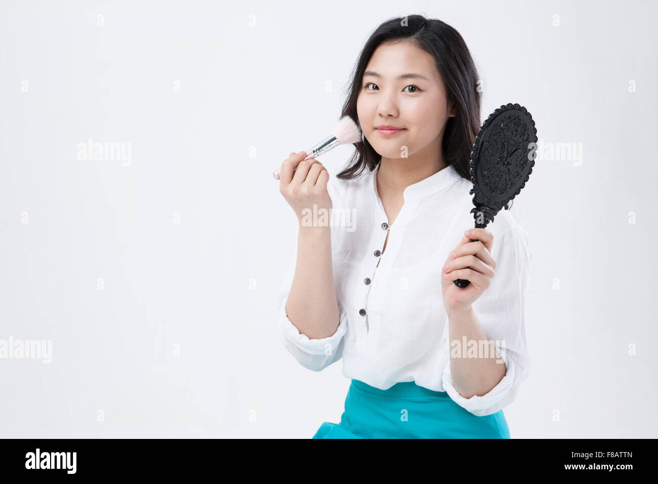 Portrait of young woman applying make up staring at front with a smile ...