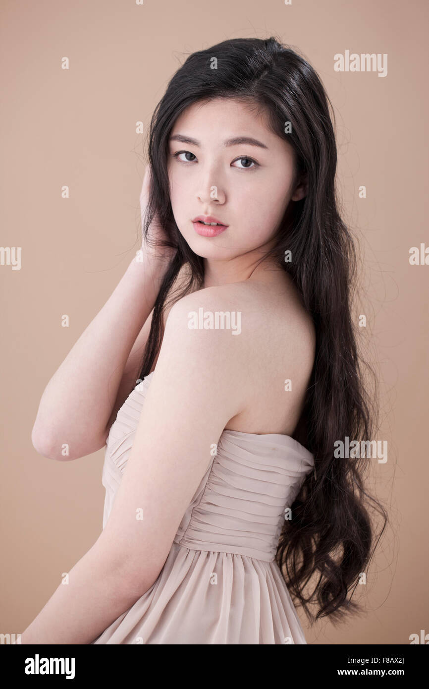 Side view of young woman with long wavy hair in dress staring at front ...