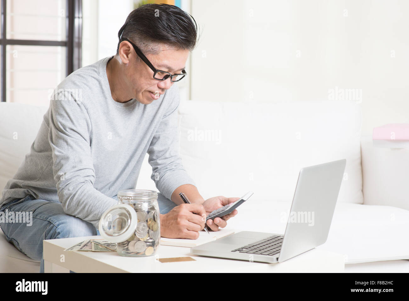 Asian mature man counting on money using calculator and laptop computer ...