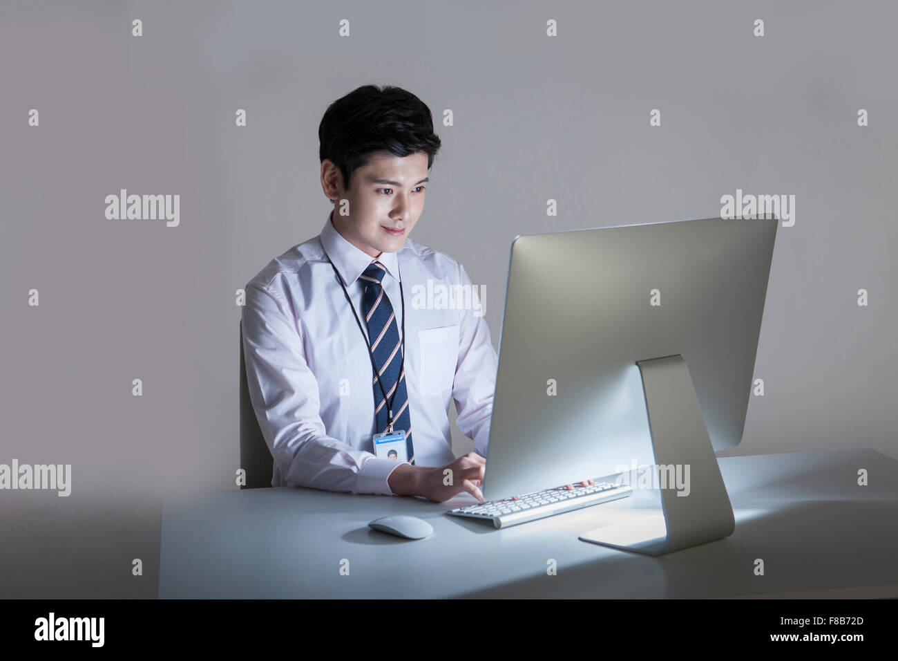 Businessman seated at desk working on computer in dark Stock Photo - Alamy