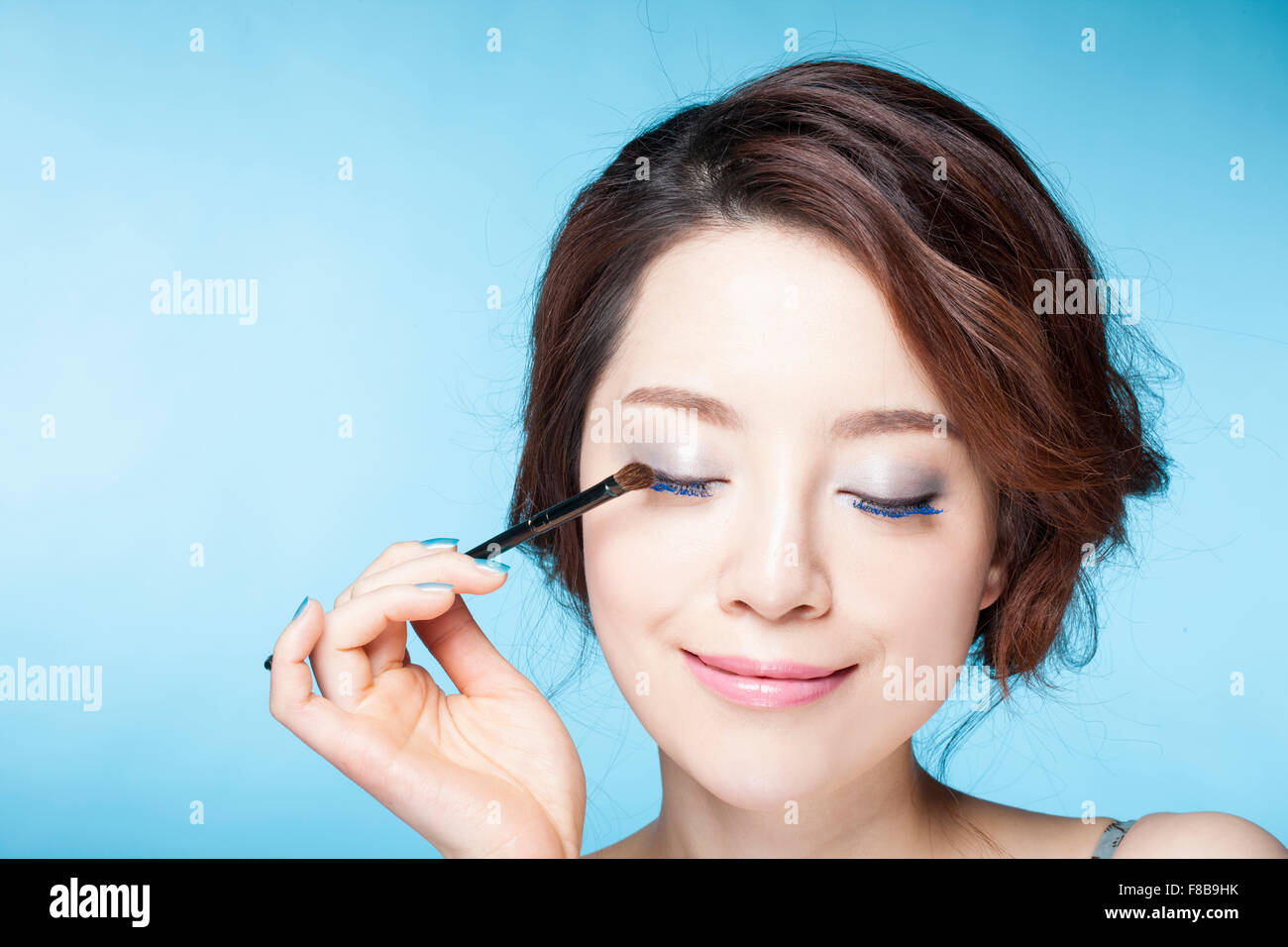 Woman with her hair up putting on eye shadow on her eye lid with her ...