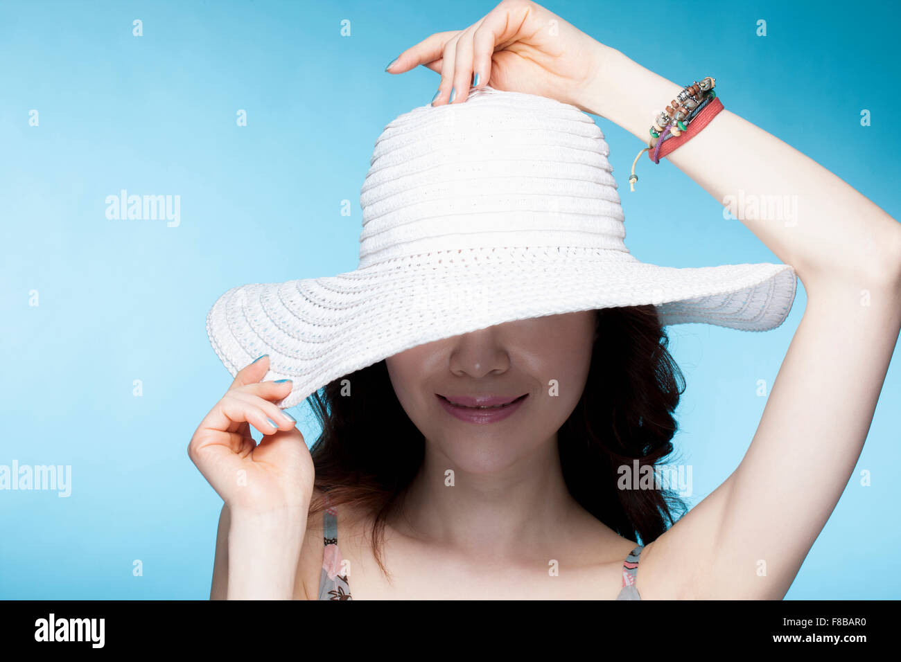 Asian woman pull a hat over her eyes and holding it with the other hand ...
