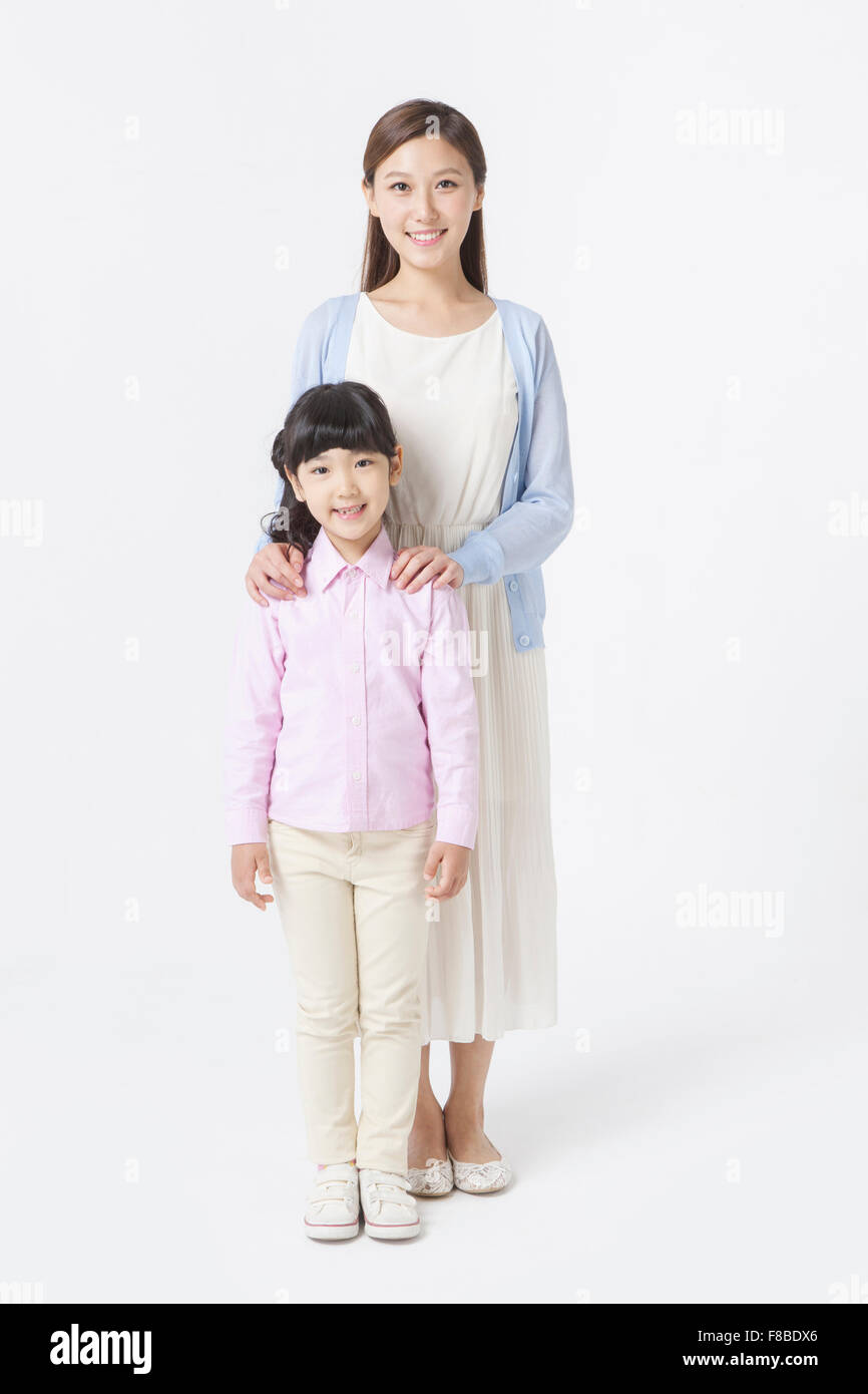 Mother standing behind her daughter both staring forward with a smile ...