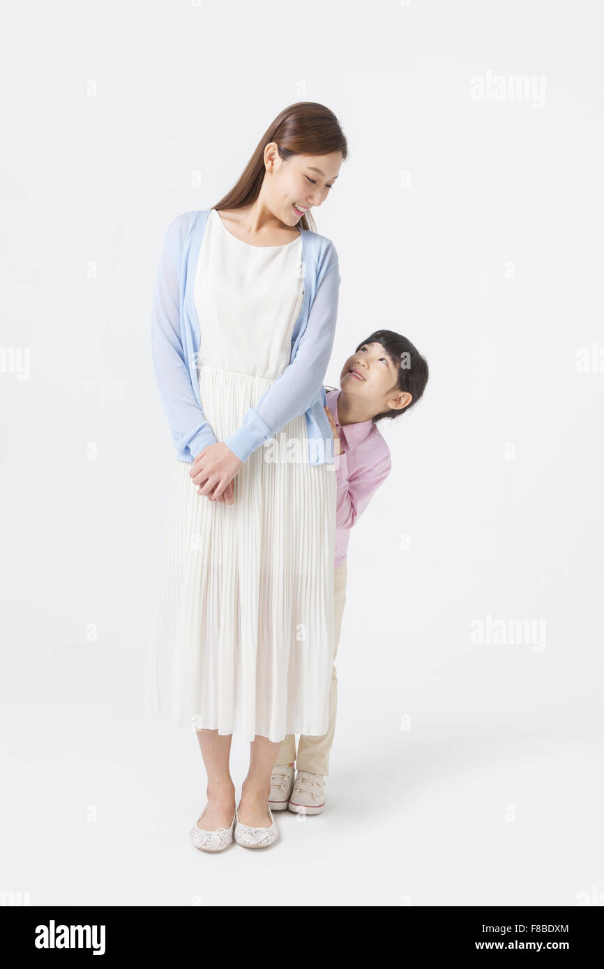 Daughter standing and hiding behind her mother and mother looking at ...