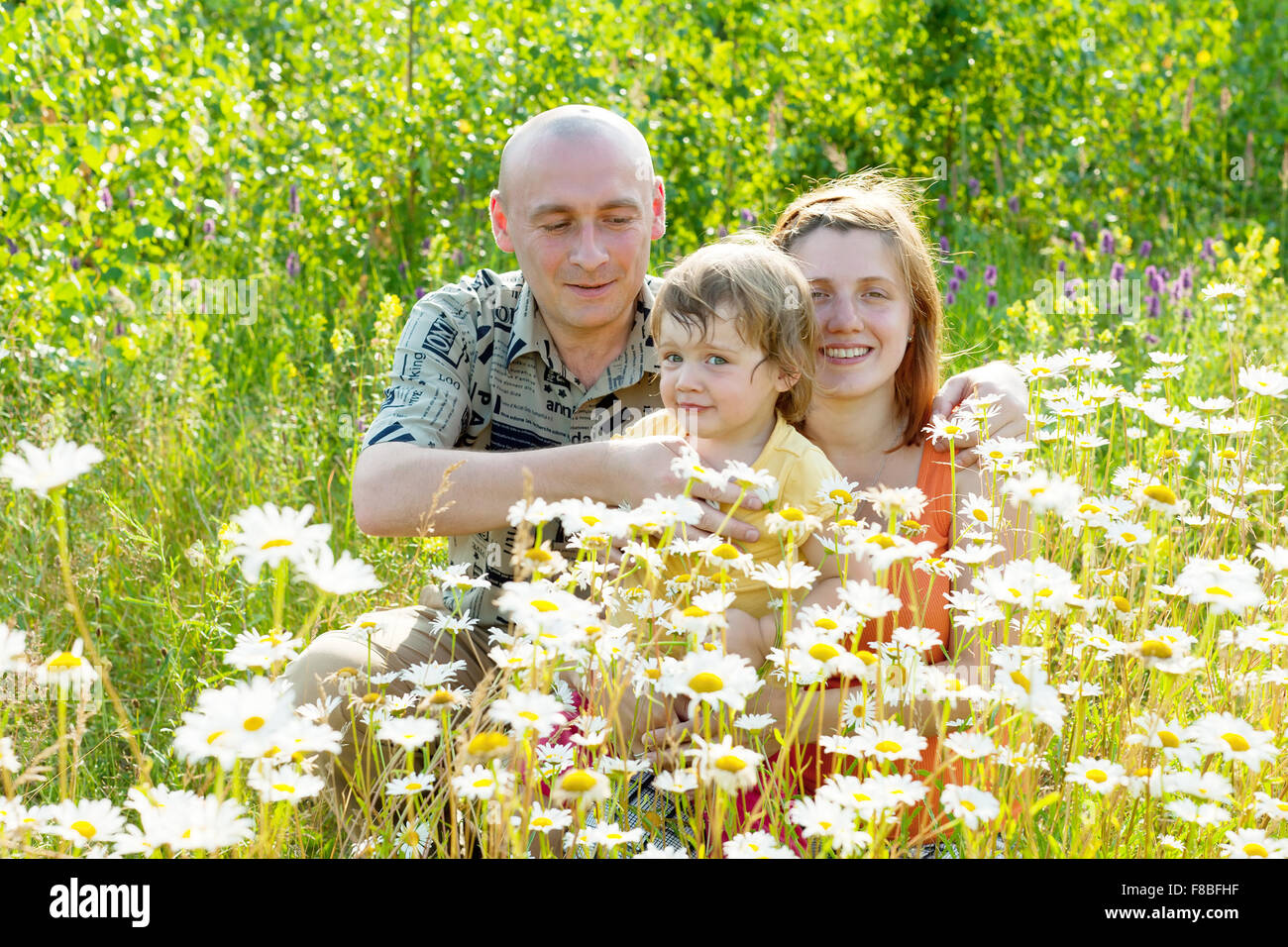 Happy parents with child sits in summer daisy plant Stock Photo - Alamy