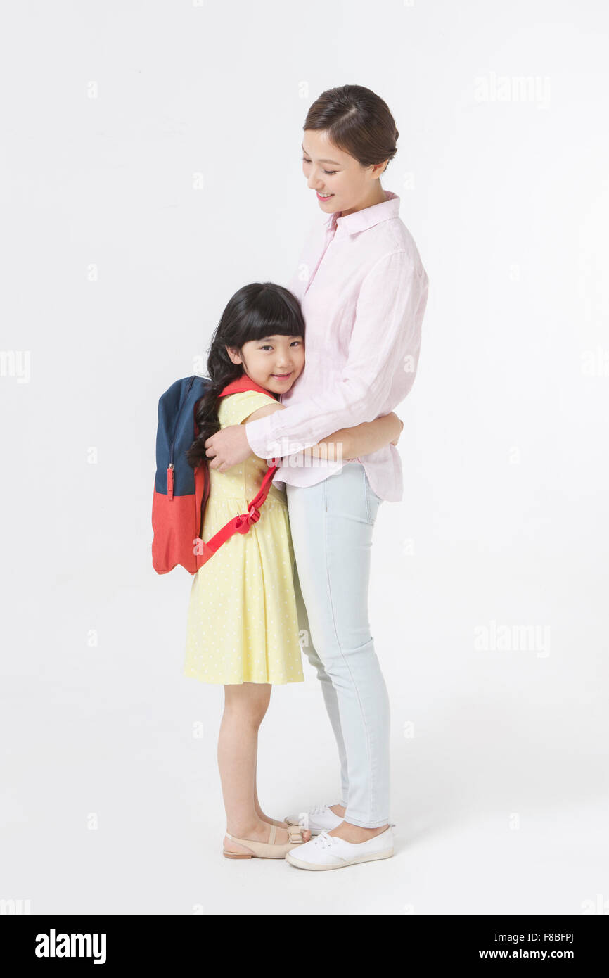 Young girl with backpack hugging her mother and staring forward with a ...