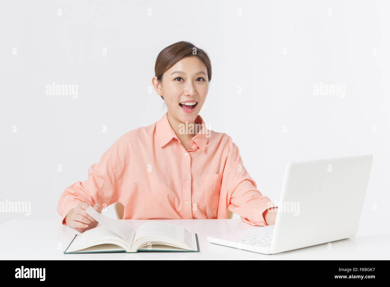 Adult woman in orange shirt seated at desk with laptop and book staring ...