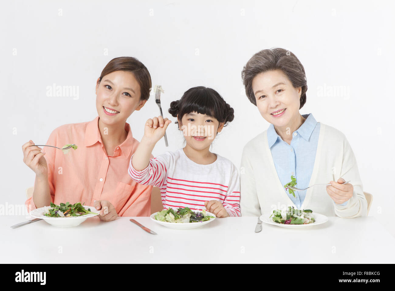 Young girl, her mother, and her grandmother seated at table and eating ...