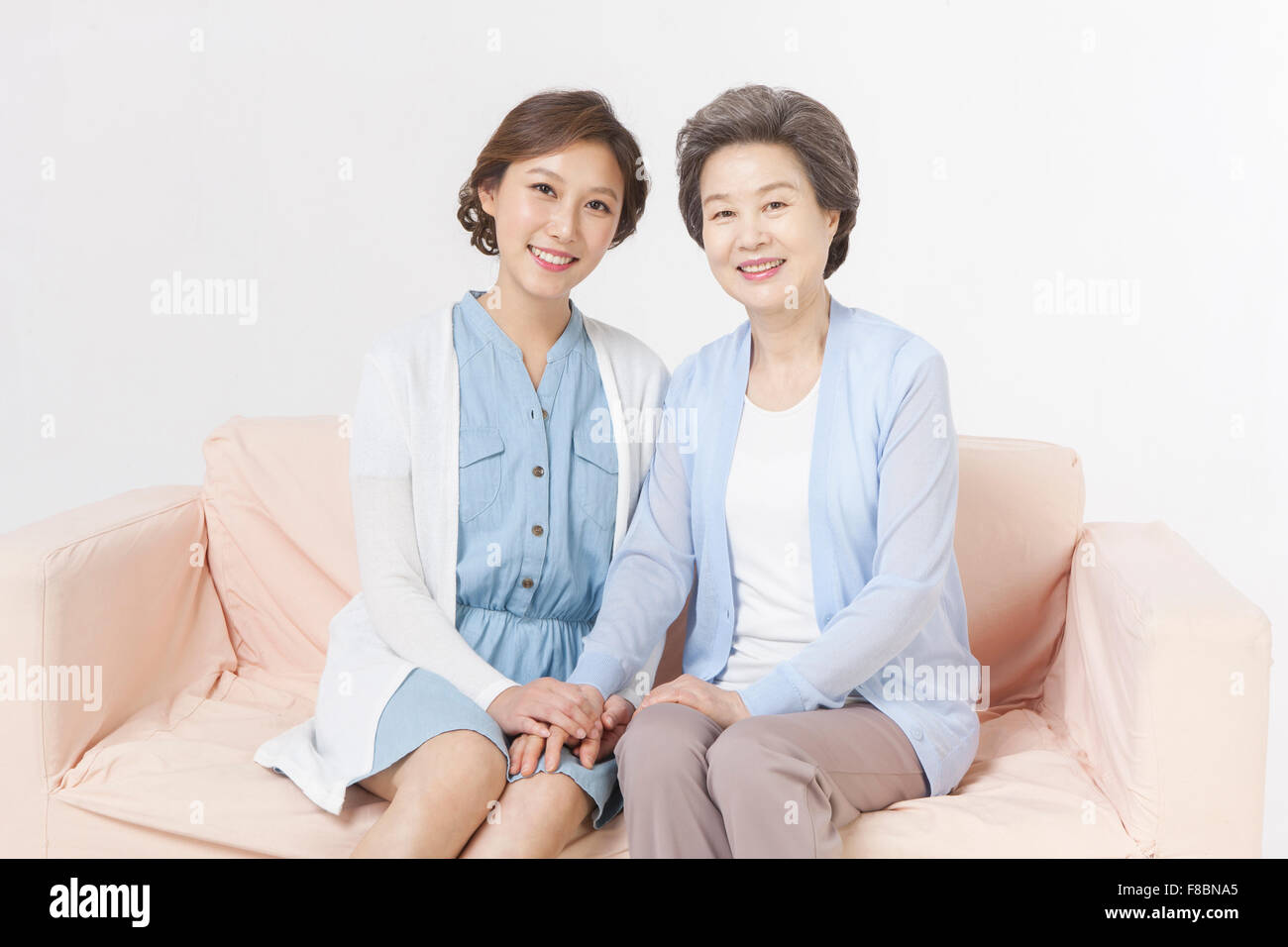 Mother and daughter sitting on a couch and staring forward with a smile ...