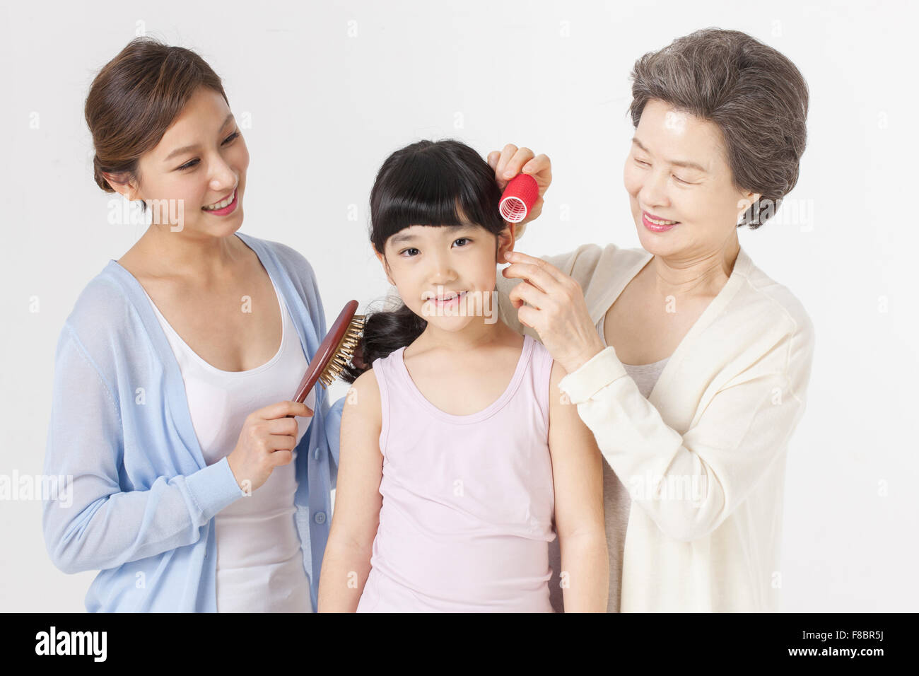 Young girl getting hair style by her mother and grandmother holding ...