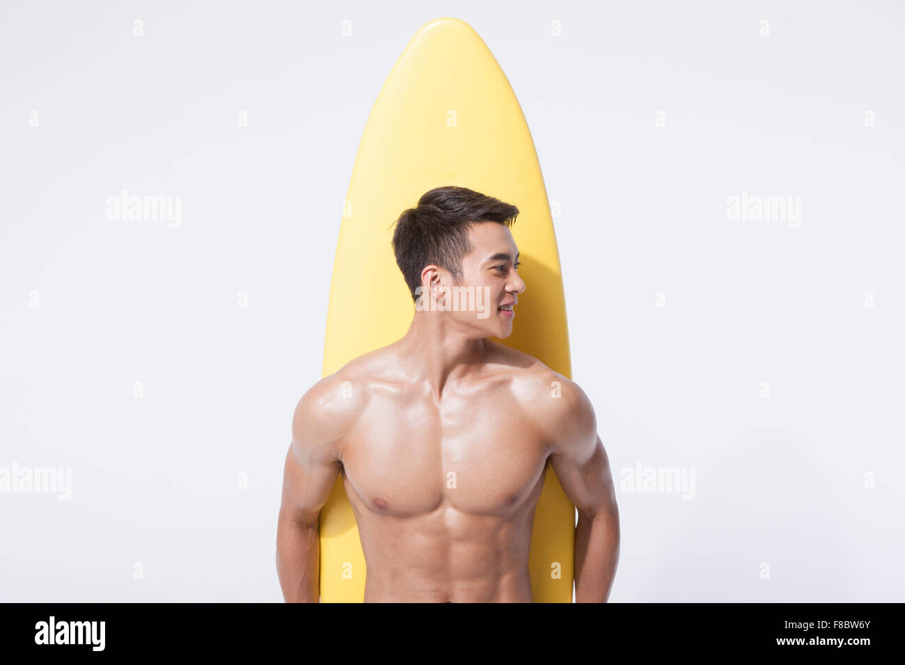 Muscular man holding yellow surfing board behind his back Stock Photo ...