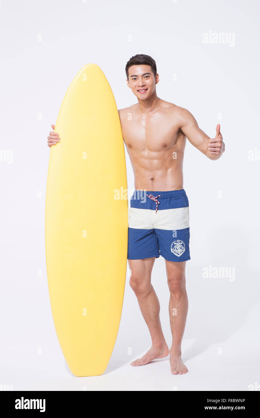 Muscular man standing and holding a surfing board next to him with his ...