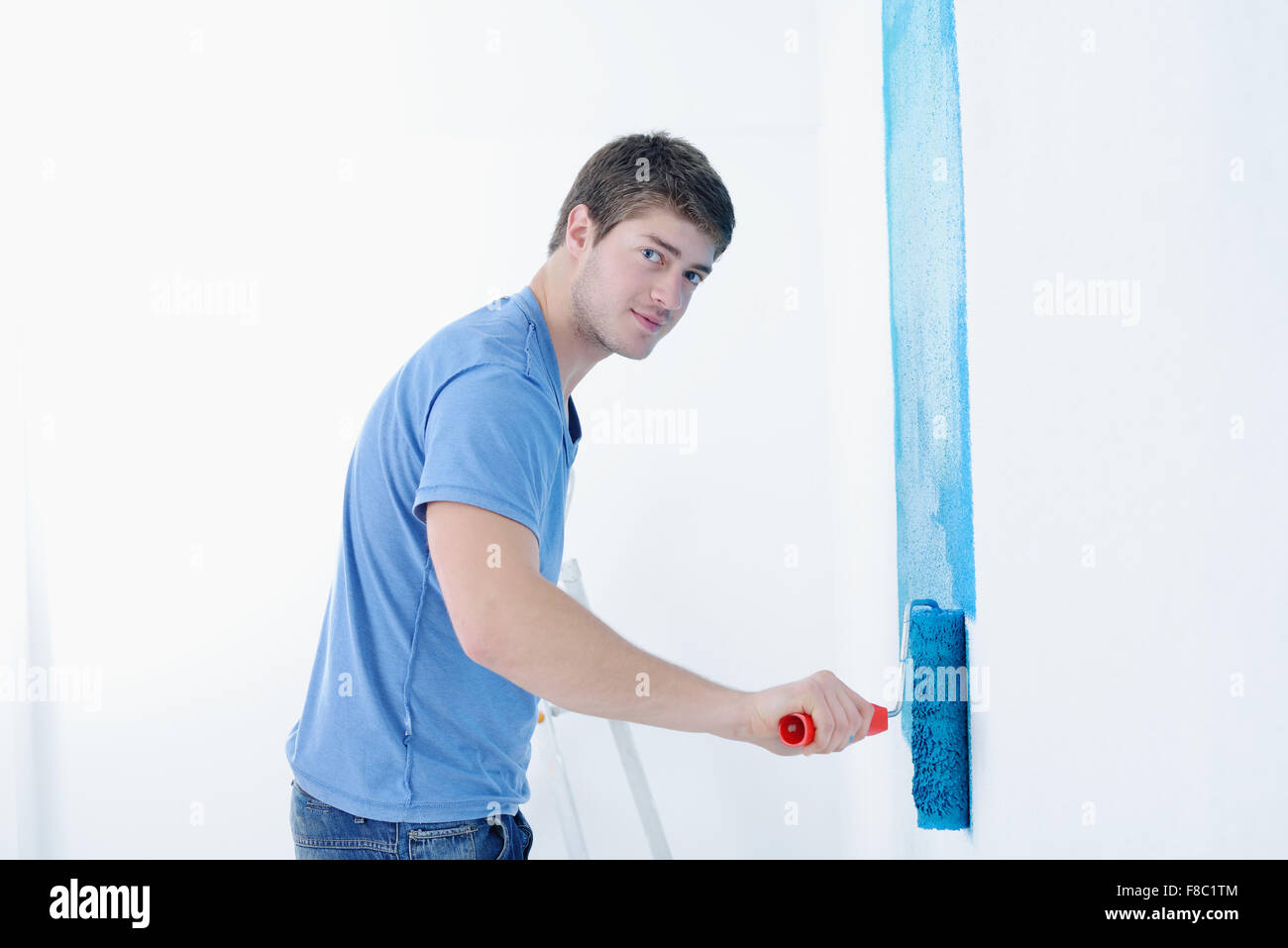 handsome young man paint in blue and green color white wall of new home ...