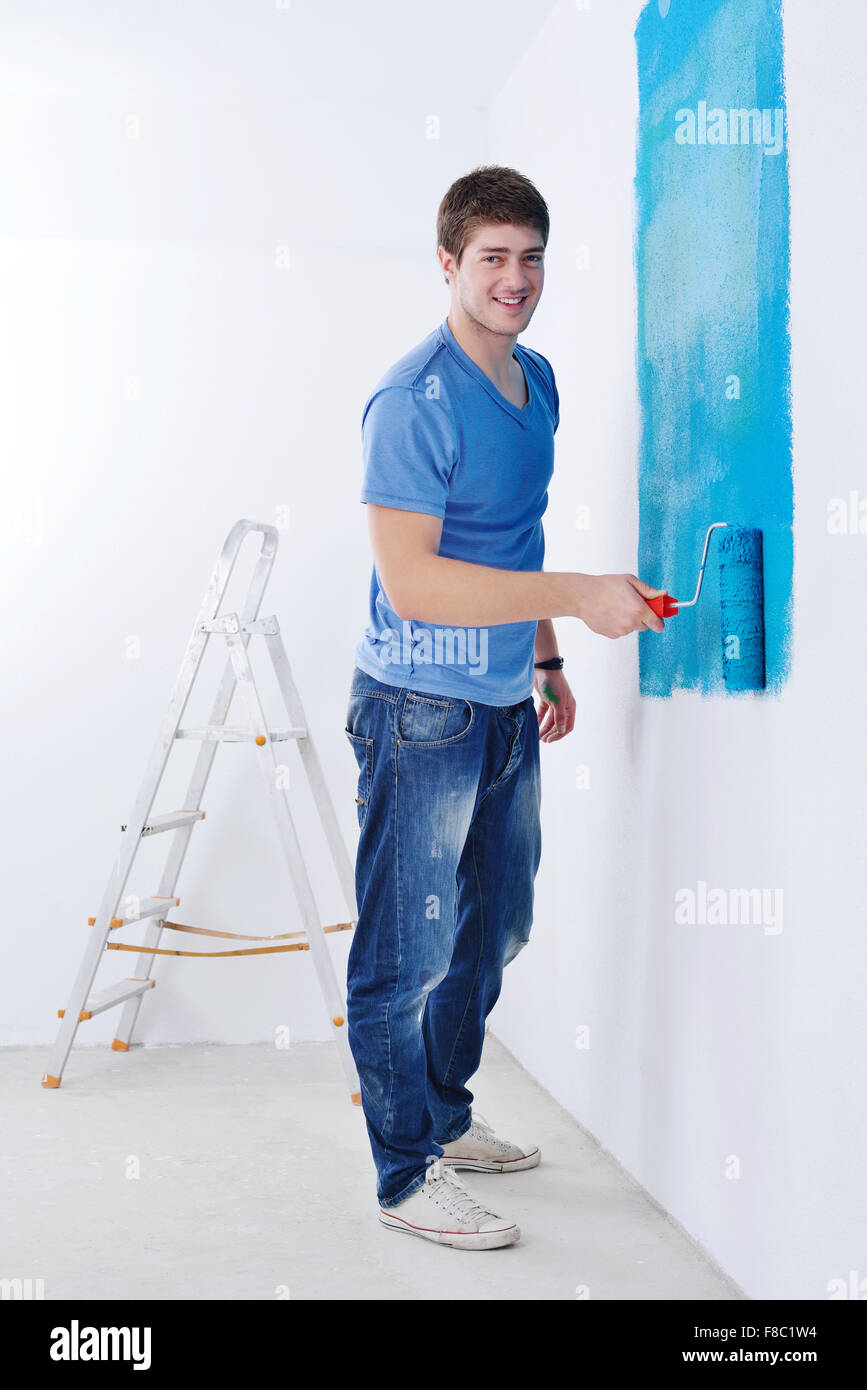 handsome young man paint in blue and green color white wall of new home ...