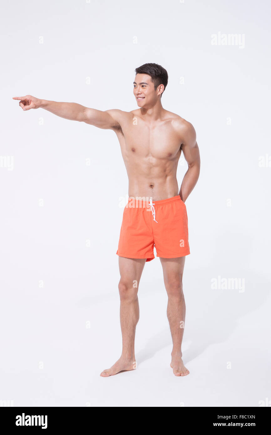 Muscular man in swimming pants standing and pointing somewhere with his ...