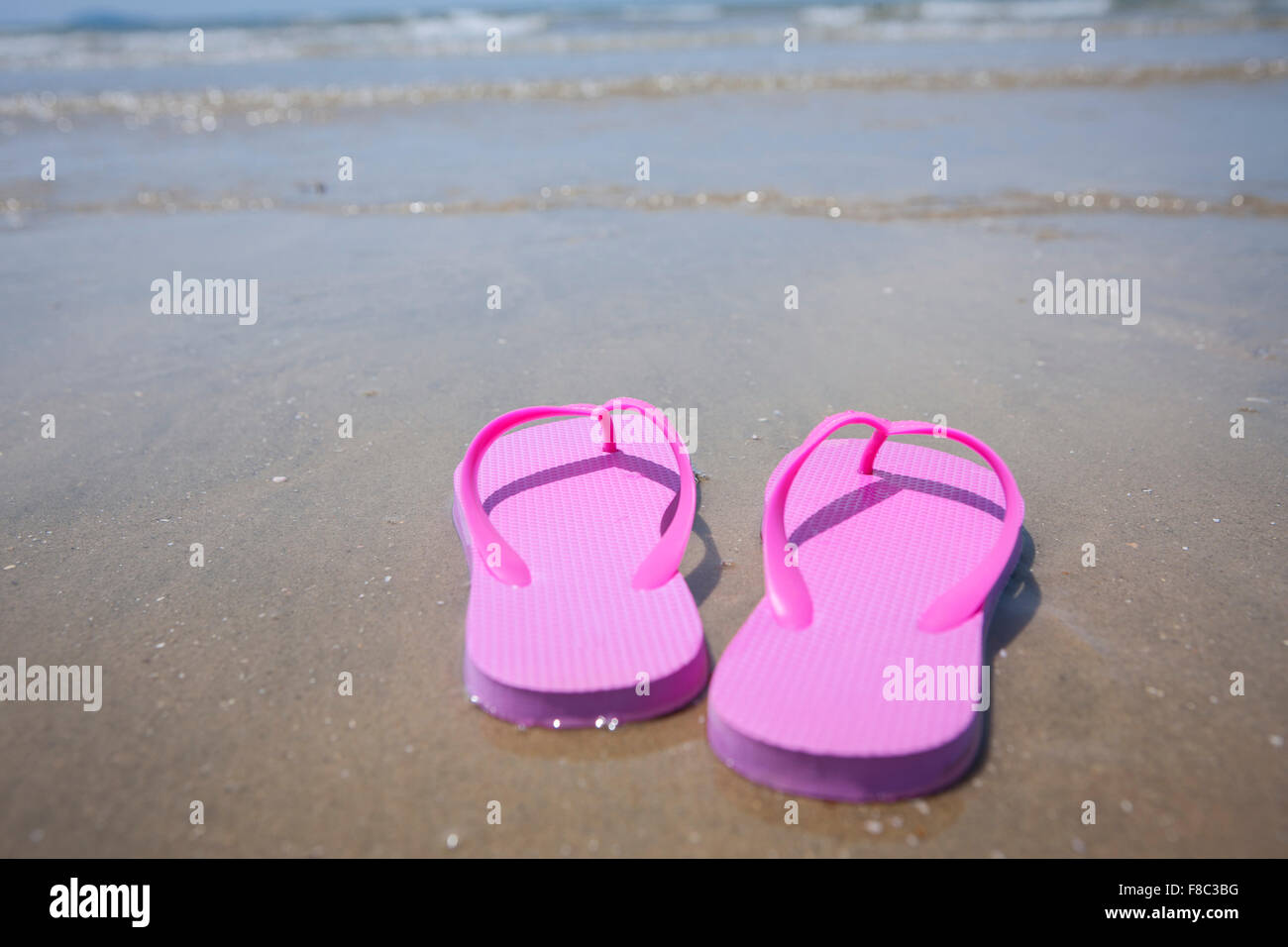 Pink flip flops on wet sand in out-focused effect with the background ...