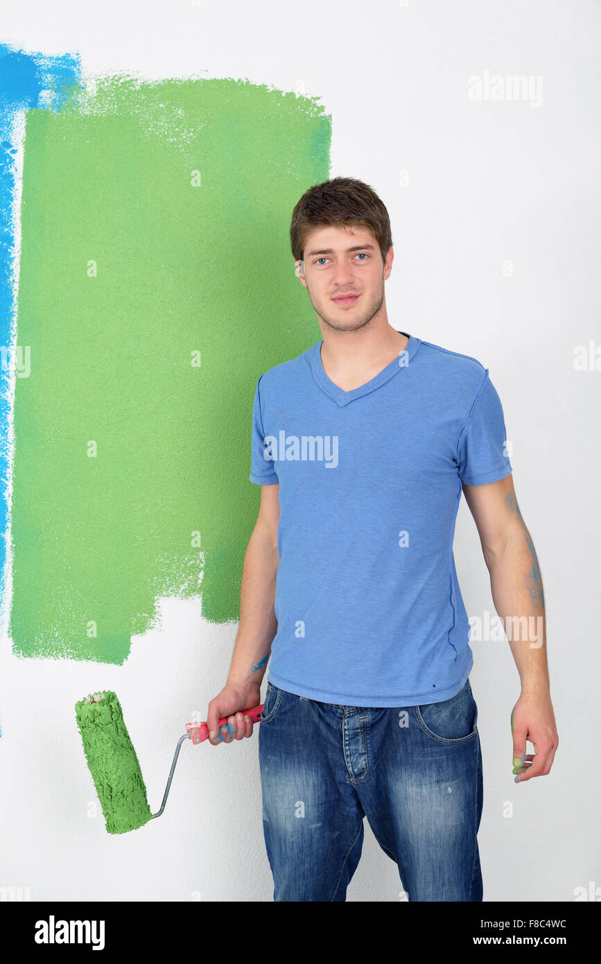 handsome young man paint in blue and green color white wall of new home ...