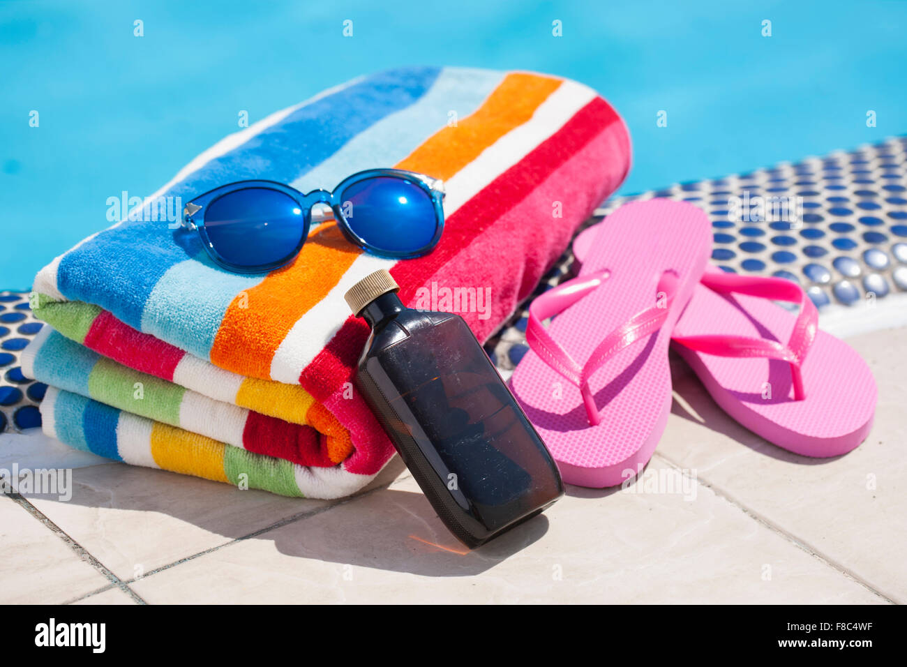 Sunglasses and tanning oil on folded towel and flip flops out of focus ...