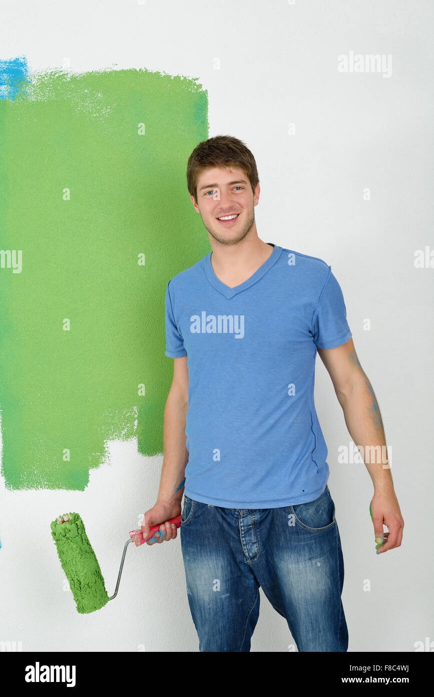 handsome young man paint in blue and green color white wall of new home ...