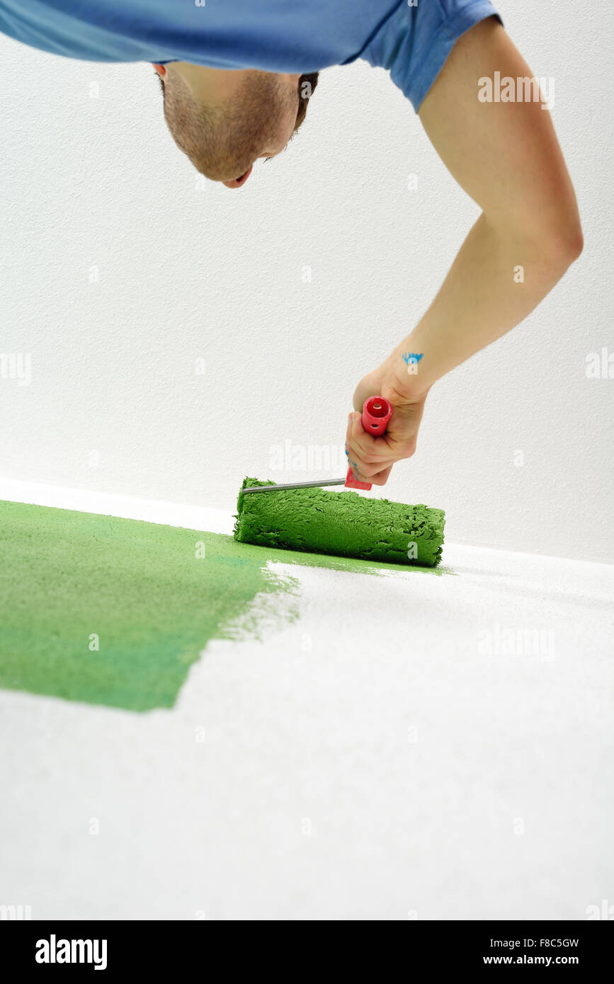 handsome young man paint in blue and green color white wall of new home ...