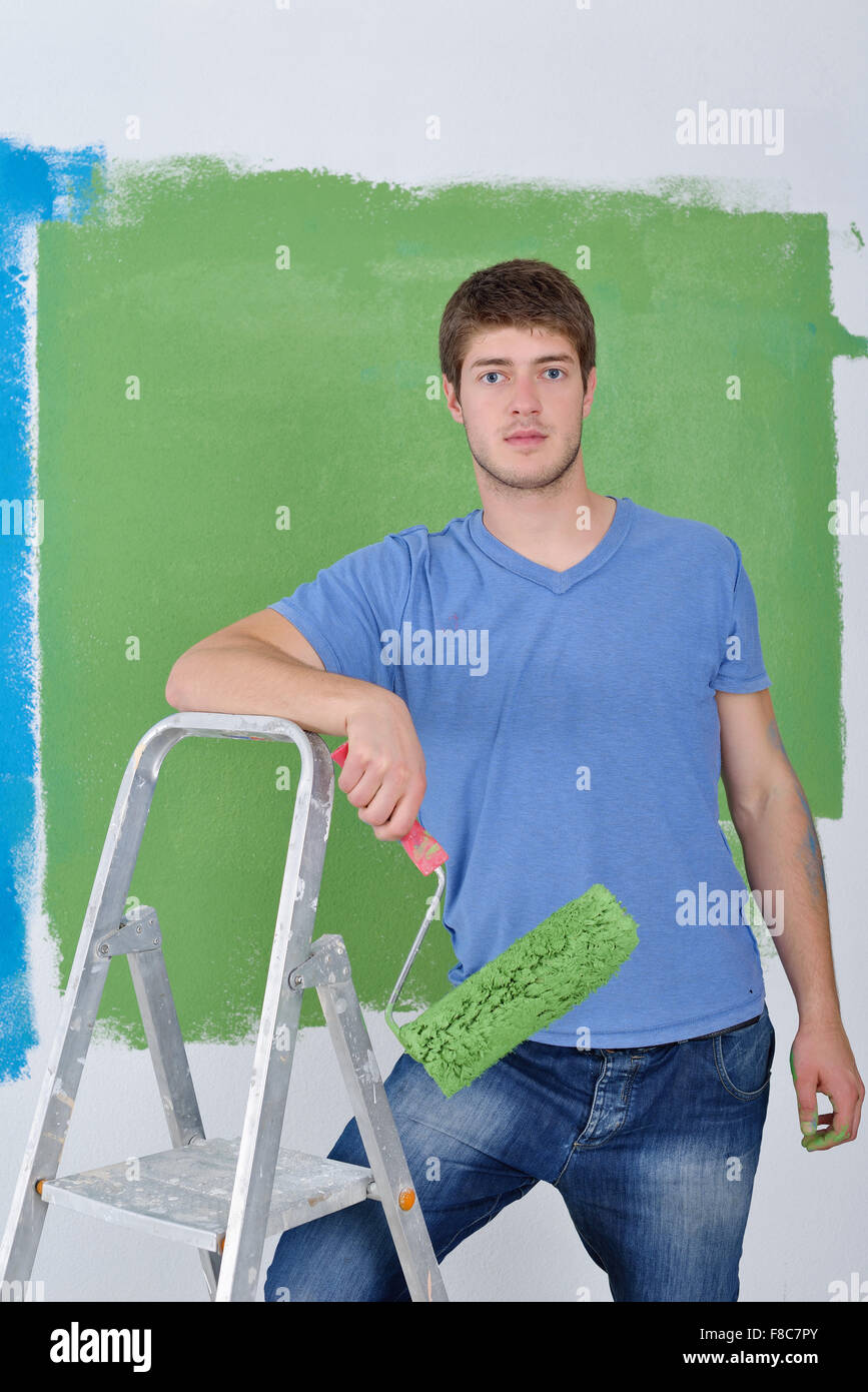 handsome young man paint in blue and green color white wall of new home ...