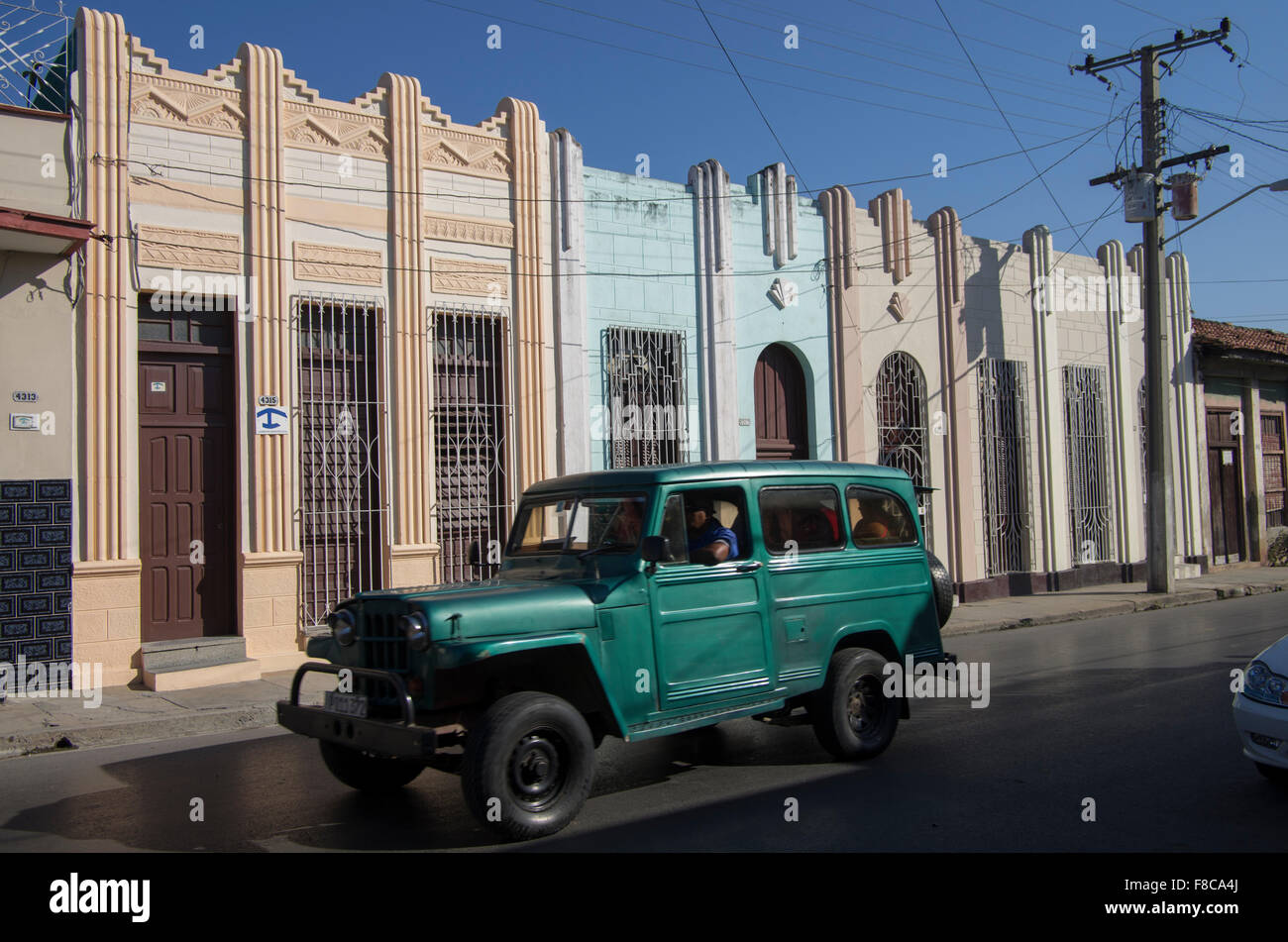 A green jeep or landrover passes art deco buildings in Cienfuegos, Cuba ...