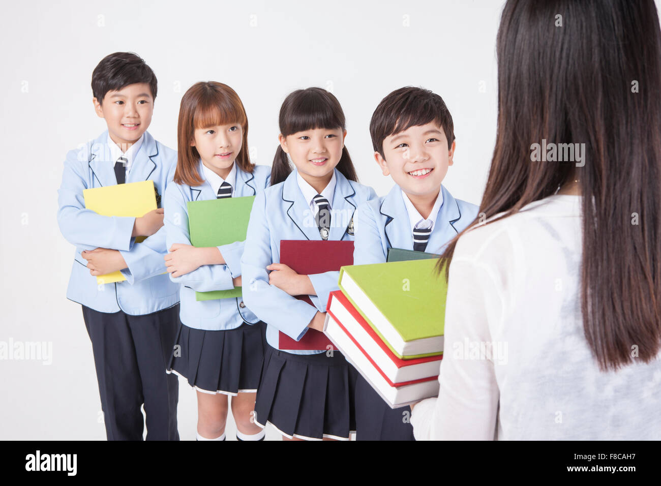 Back appearance of a teacher holding books and four elementary students ...