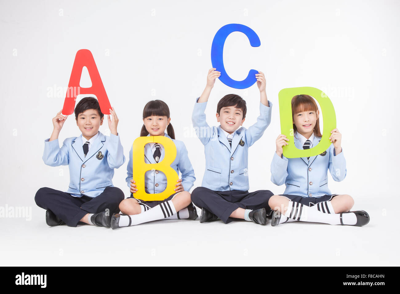 Four elementary students in school uniforms sitting and holding an ...