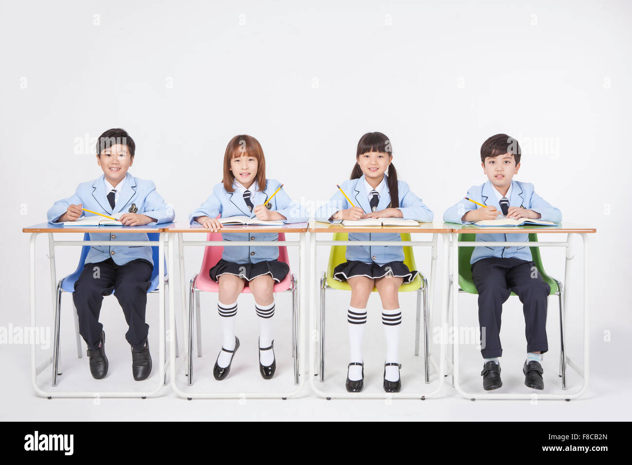 Four elementary students in school uniforms seated at desk holding a ...