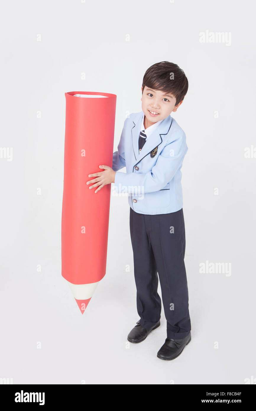 Elementary school age boy holding a big red pencil and standing with it ...